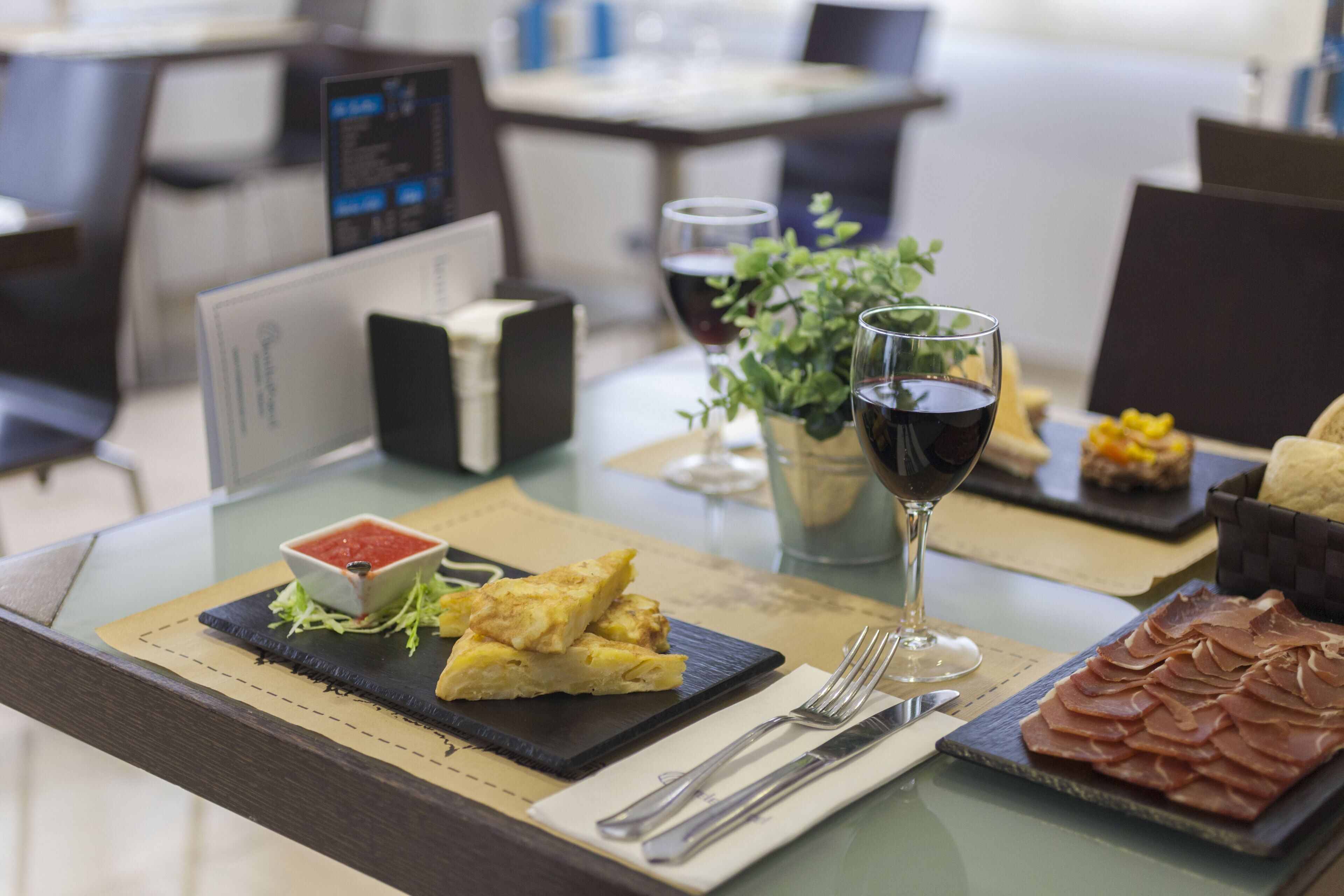 Uma mesa de jantar com diversos alimentos, incluindo um prato de carne fatiada, um copo de vinho tinto e uma pequena tigela de molho.