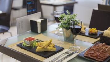 Uma mesa de jantar com diversos alimentos, incluindo um prato de carne fatiada, um copo de vinho tinto e uma pequena tigela de molho.