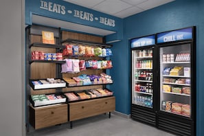 Exposição de lanches com diversos alimentos embalados e um refrigerador para bebidas geladas.
