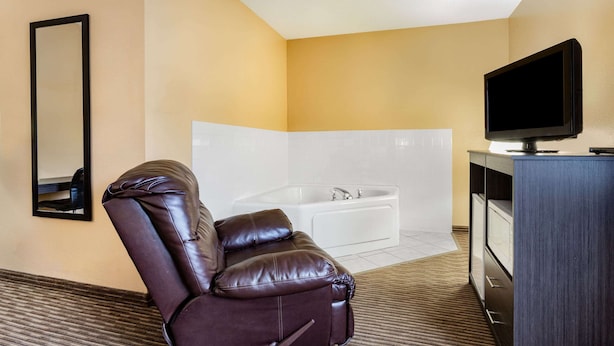 Quarto de hotel com poltrona de couro reclinável, televisão de tela plana, banheira branca e um espelho grande.