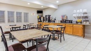 Um restaurante com várias mesas e cadeiras, uma área de cozinha com eletrodomésticos e um balcão com pratos e temperos.