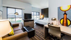 Quarto de hotel com cama, escrivaninha, cadeira e televisão.
