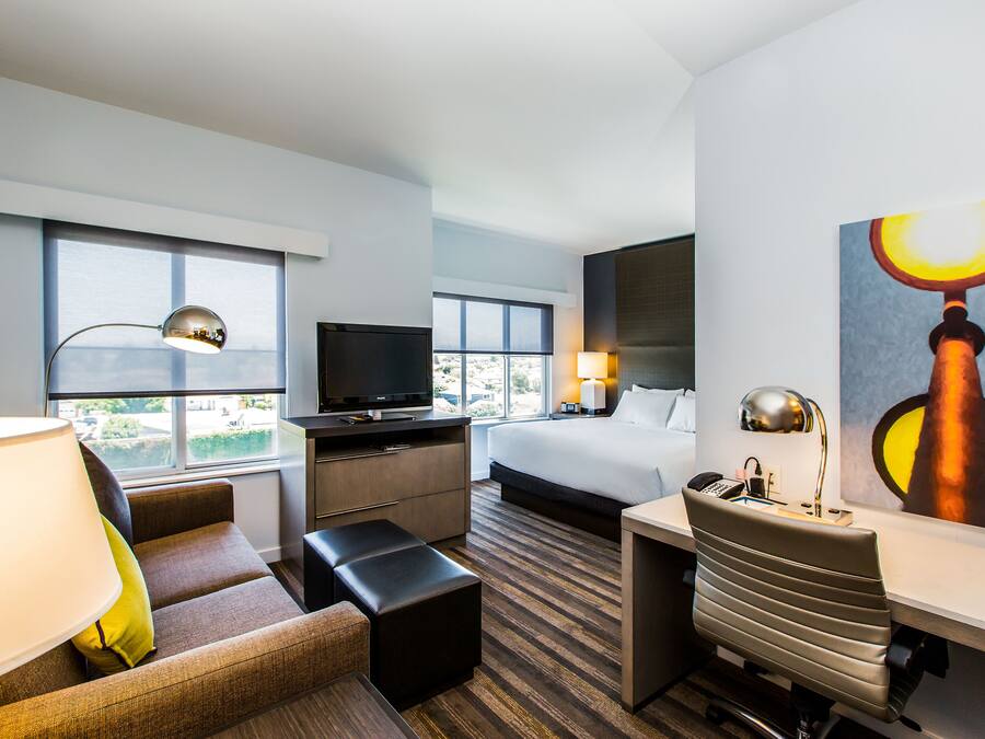 Quarto de hotel com cama, escrivaninha, cadeira e televisão.