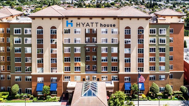 Um hotel com vários andares, um letreiro chamativo de 'HYATT House', grandes janelas e uma bandeira na frente.