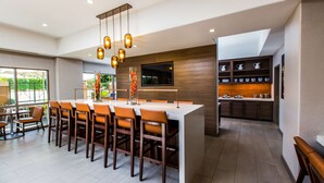 Uma cozinha moderna com uma ilha central, banquetas e uma TV fixada na parede.