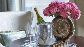 Uma mesa com uma garrafa de champanhe, dois copos, um vaso com flores cor-de-rosa e um prato com sobremesas.