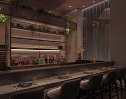 Uma área de bar com prateleiras cheias de garrafas de bebidas, copos e um vaso de planta.