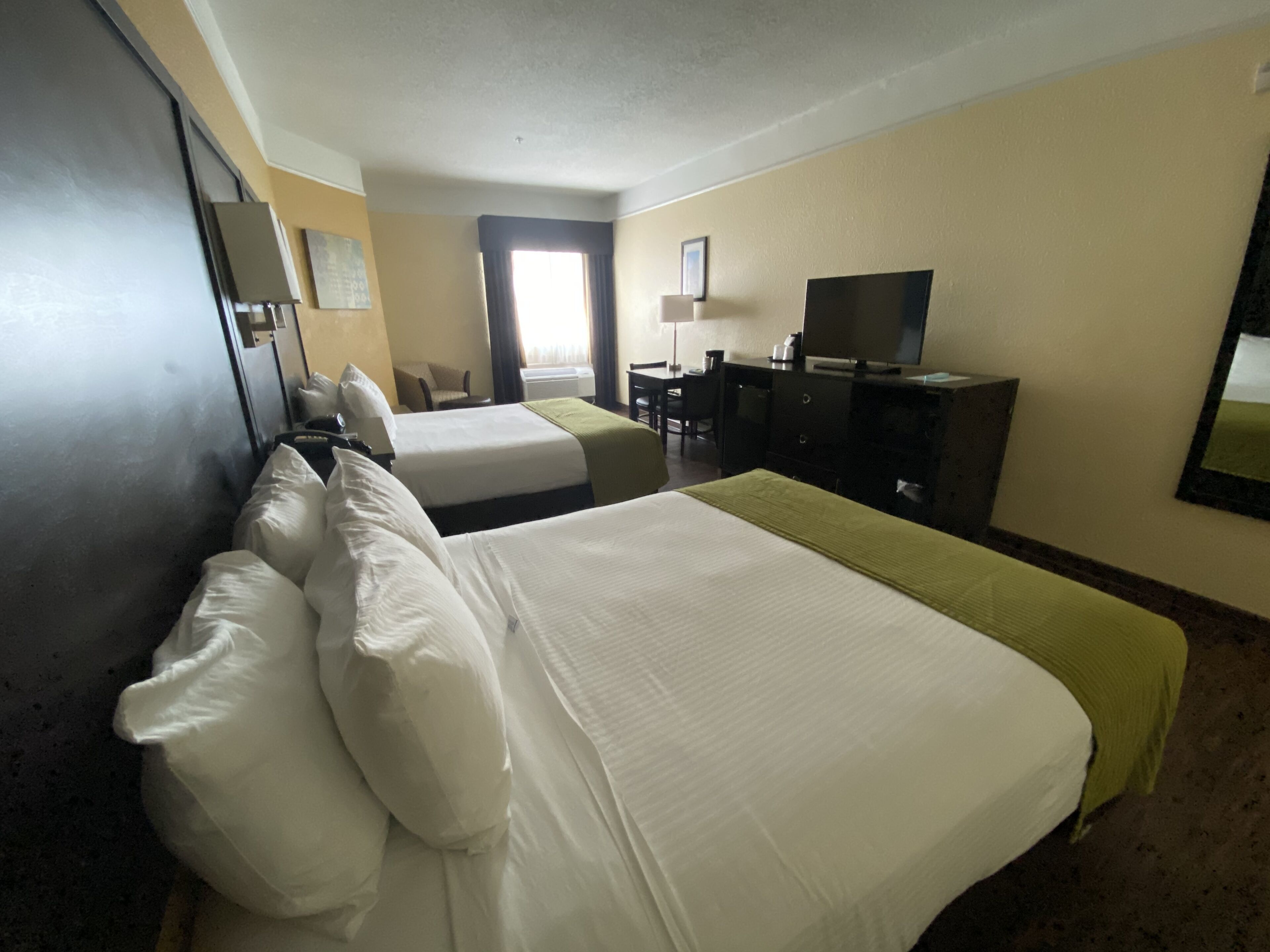 Quarto de hotel com duas camas, uma escrivaninha, uma cadeira, uma televisão e um espelho.