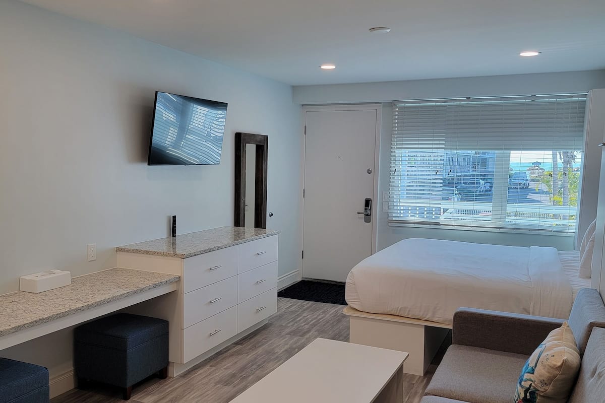 Quarto moderno com cama, televisão, escrivaninha e janela com persianas.