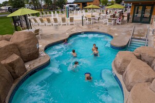 Piscina com formações rochosas, cadeiras de sol e guarda-sóis.