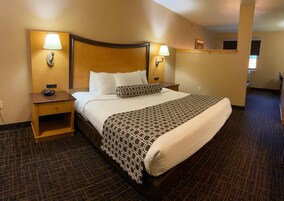 Quarto de hotel com uma cama grande, duas luminárias de cabeceira, uma mesinha de cabeceira e uma pequena escrivaninha.