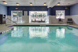 Piscina com superfície de água cristalina, área de estar à beira da piscina e vista para o exterior através de uma porta de vidro.