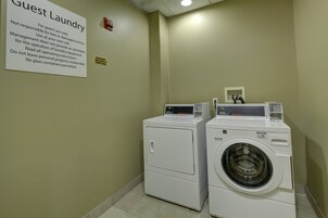 Área de lavanderia para hóspedes, com duas máquinas de lavar e um aviso com instruções.