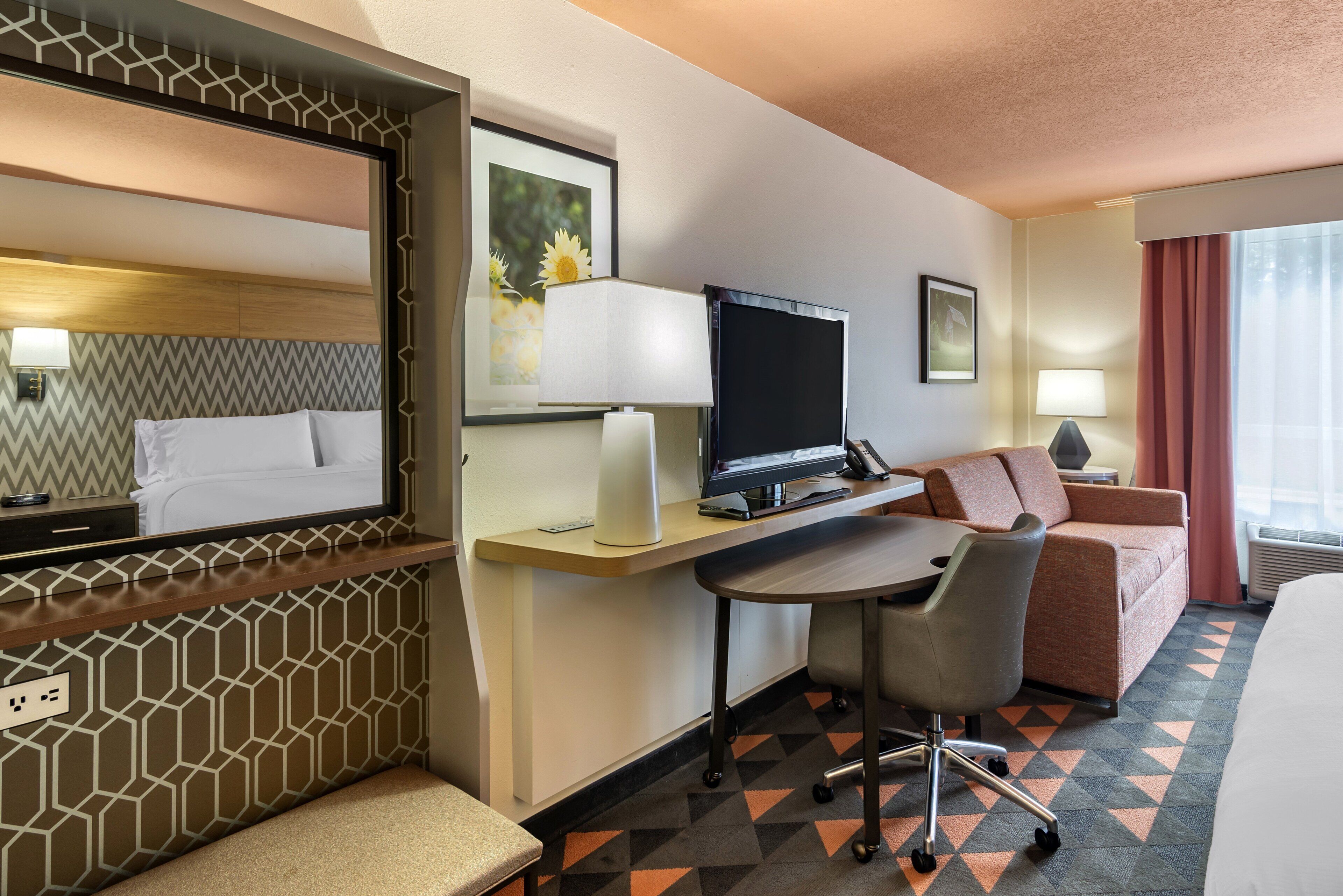Quarto de hotel com cama, escrivaninha, cadeira e sofá.