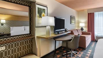 Quarto de hotel com cama, escrivaninha, cadeira e sofá.