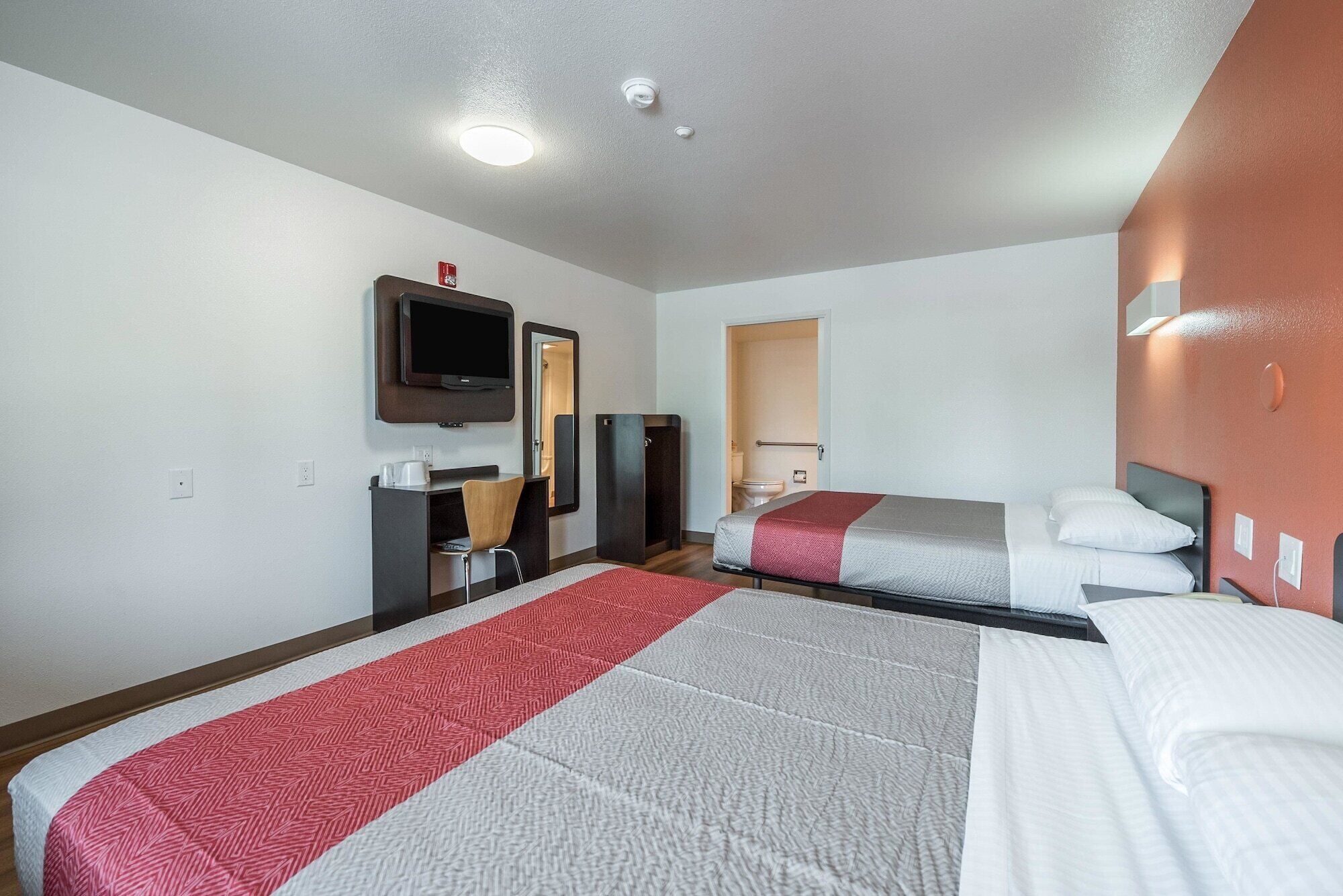 Quarto de hotel com duas camas, televisão, secretária e espelho.