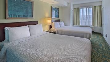 Quarto de hotel com duas camas, uma janela grande com cortinas, um quadro na parede e piso coberto por carpete.