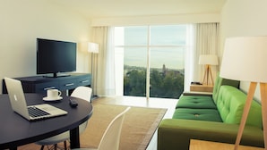 Quarto de hotel com escrivaninha, laptop, comando remoto e sofá verde.