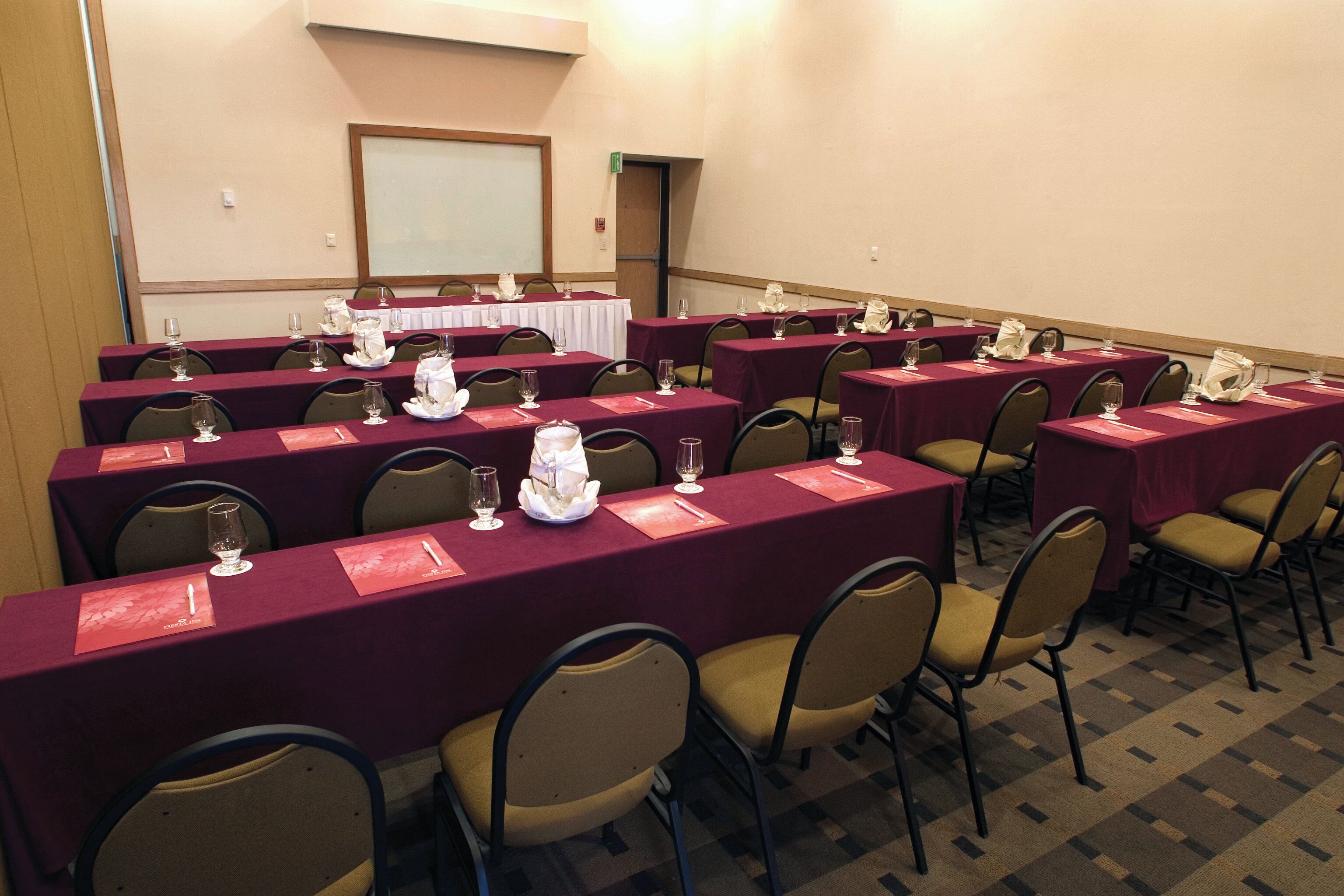 Sala de conferências com várias mesas preparadas para reuniões, equipada com cadeiras e copos.