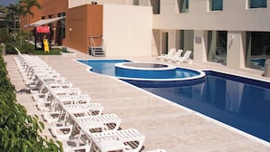 Hotel com piscina, espreguiçadeiras e uma palmeira.