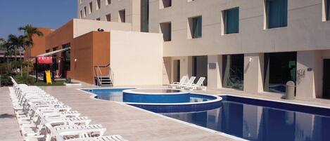 Uma área de piscina com espreguiçadeiras e um edifício com várias janelas.