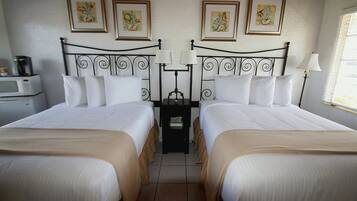 Quarto de hotel com duas camas, mesa de cabeceira, abajur e obras de arte emolduradas na parede.