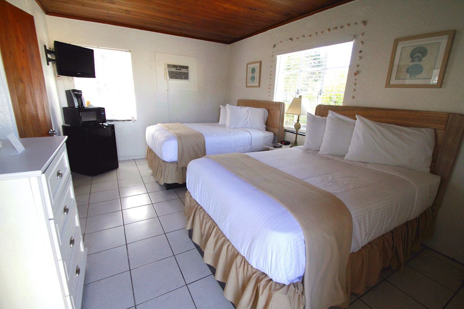Quarto de hotel com duas camas, uma escrivaninha com computador, televisão e janela com persianas.