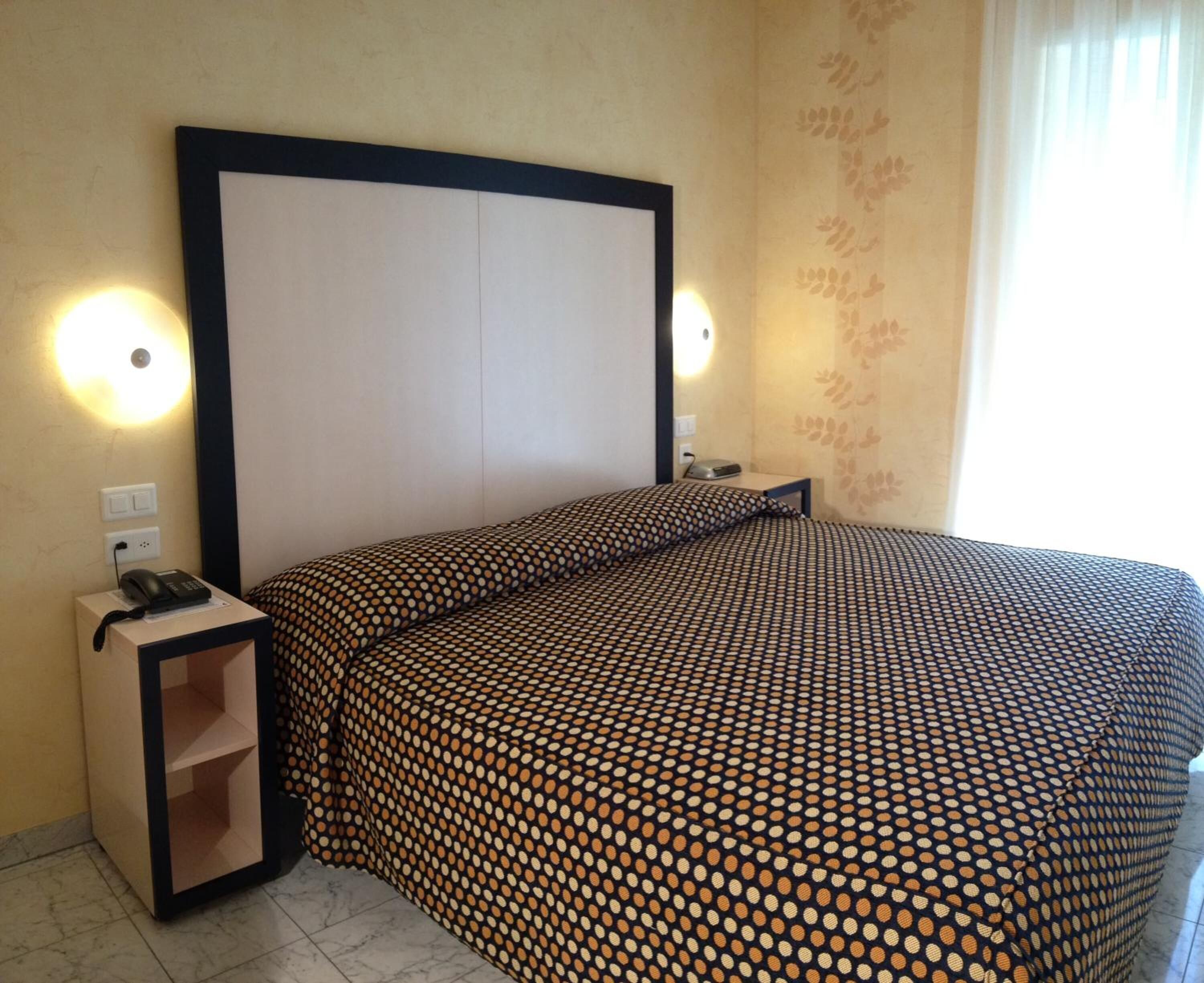 Quarto de hotel com uma cama grande, duas mesas de cabeceira e um telefone fixado na parede.