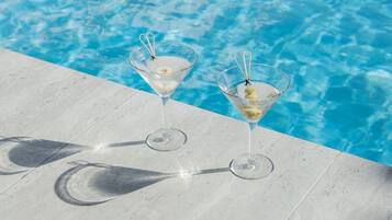 Dois copos de martini com guarda-chuvas em um deck à beira da piscina.