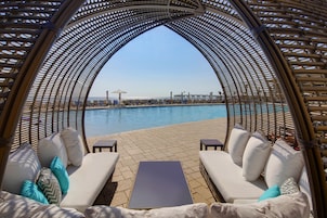 Espaço de estar semiaberto com vista para uma piscina e um cais ao longe.