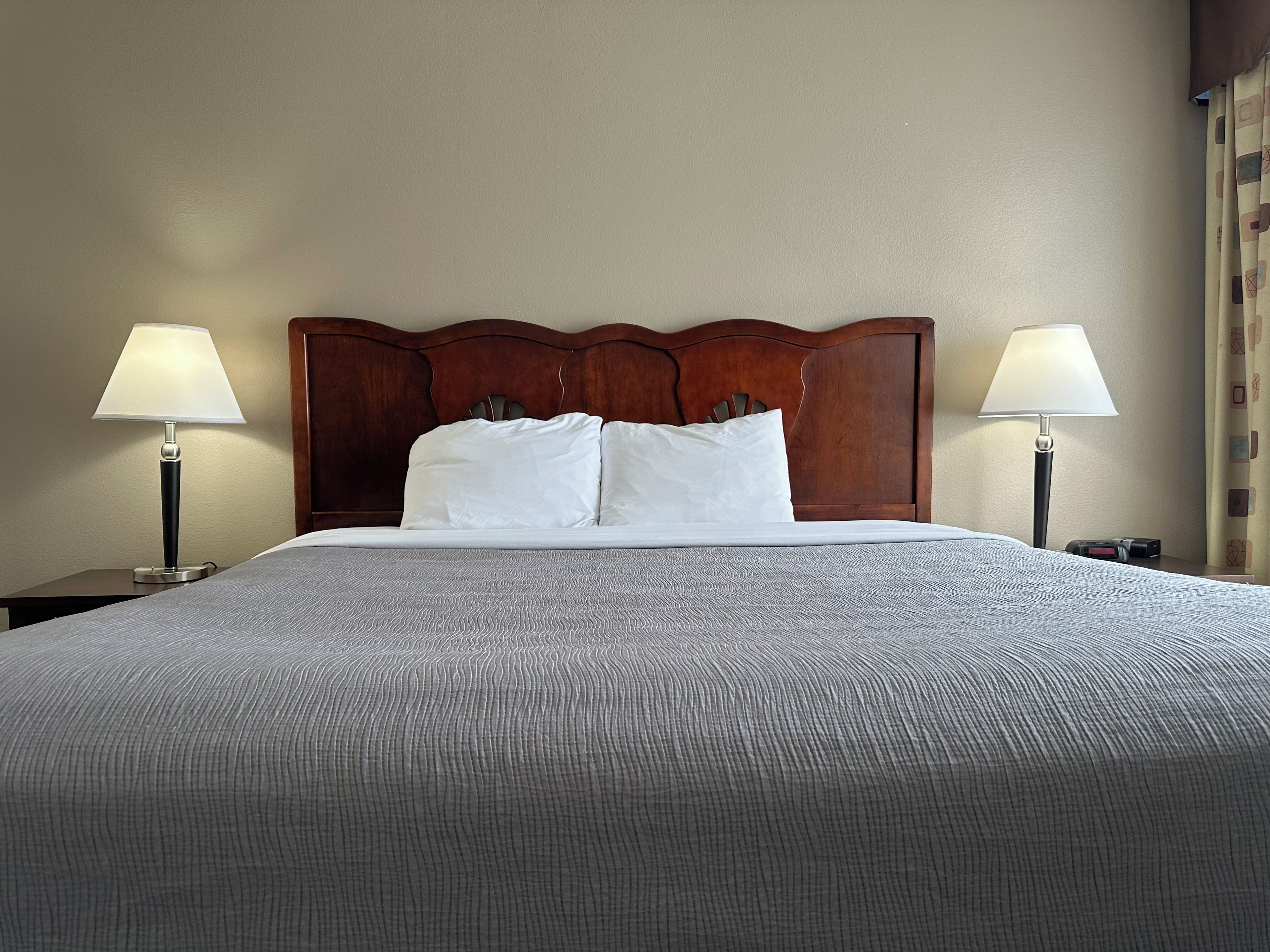 Cama bem arrumada com lençóis brancos, duas luminárias de cabeceira e cabeceira de madeira.