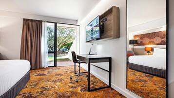 Quarto de hotel com cama, escrivaninha com cadeira, televisão na parede e um espelho grande refletindo o ambiente.