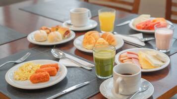 Uma mesa de café da manhã com pratos de ovos, croissants, presunto, queijo e suco.