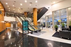 Um hall moderno com escadas rolantes, balcão de recepção e entrada de vidro.