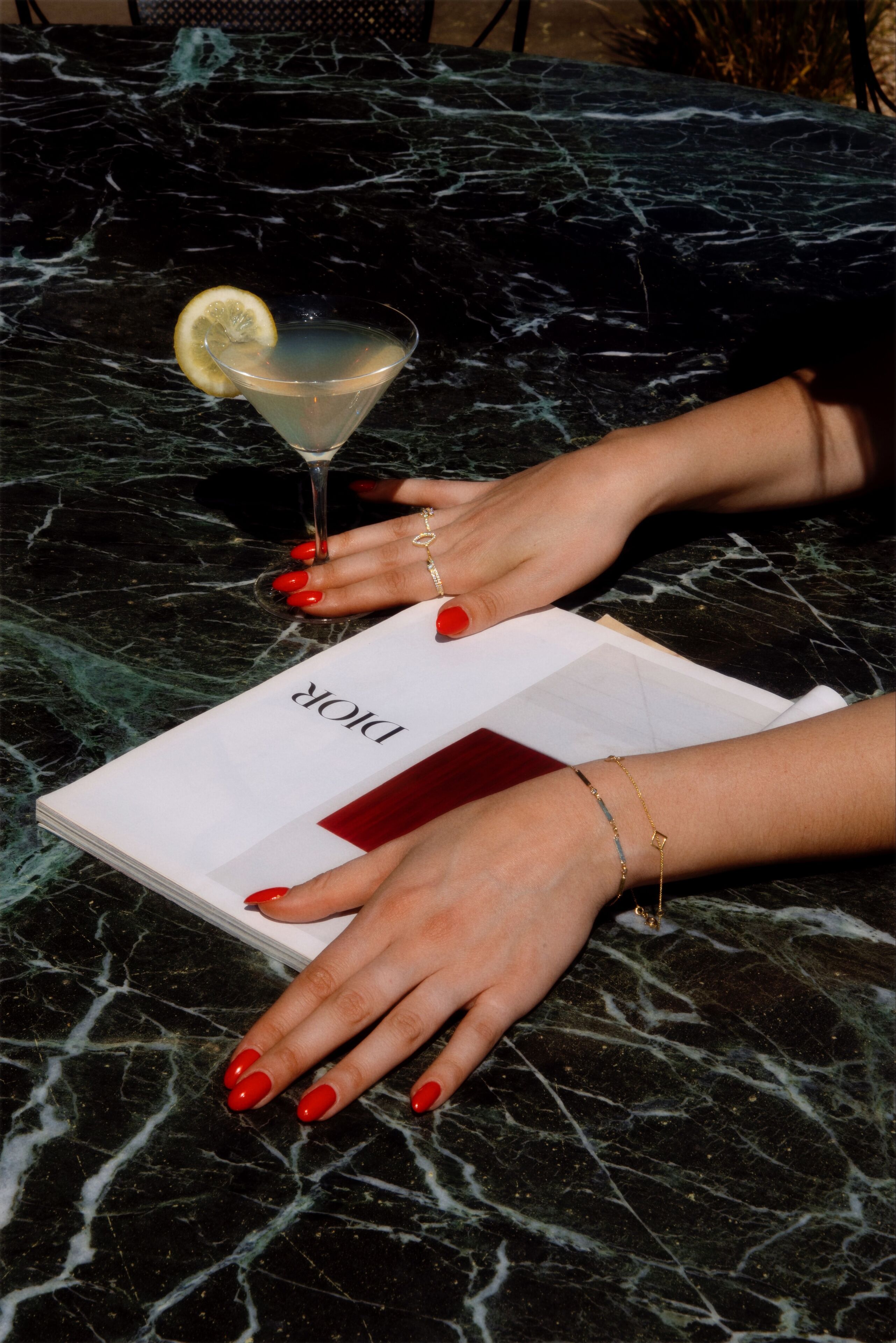 Um livro com o título "Dior" sobre uma mesa de mármore, com uma taça de martini e uma fatia de limão.