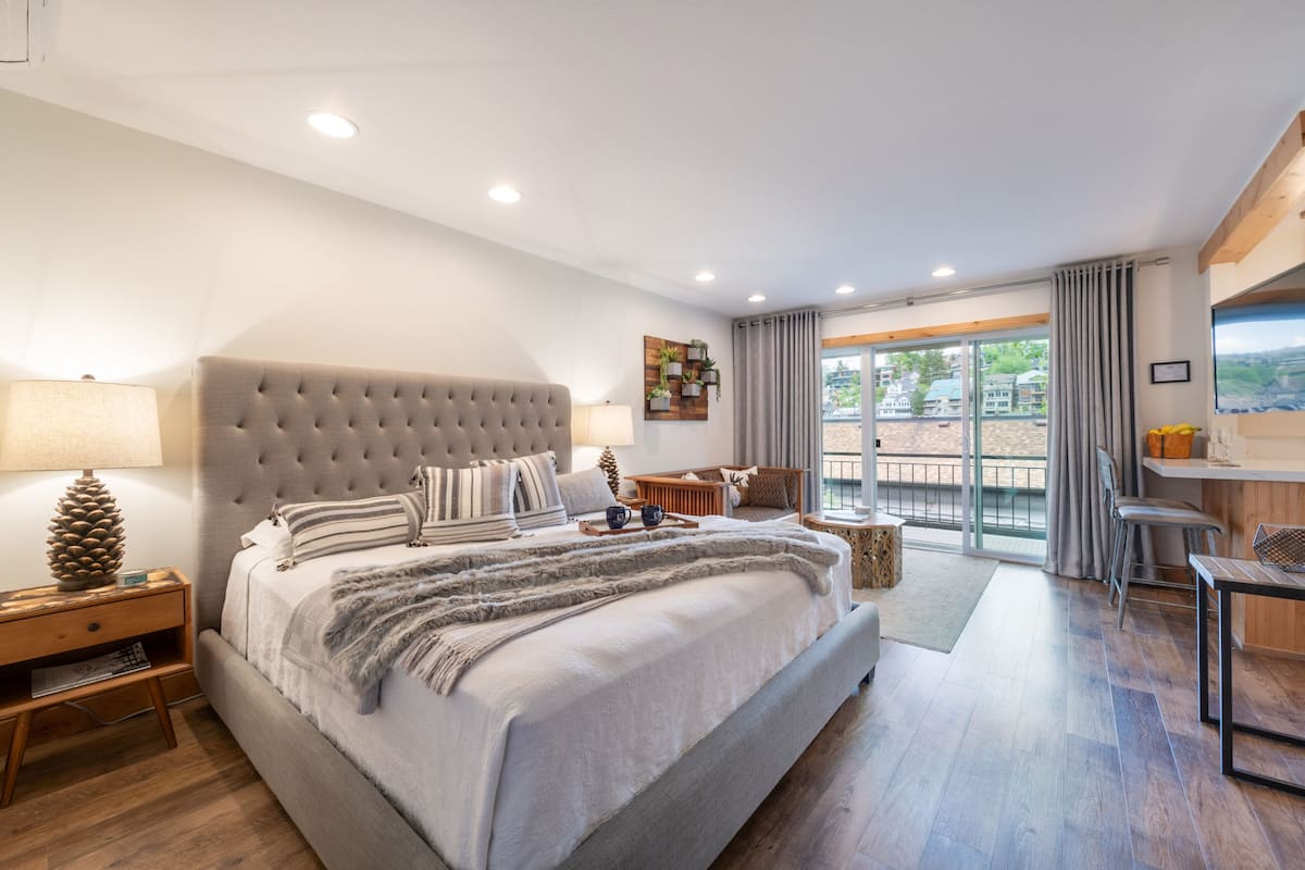 Quarto moderno com uma cama grande, mesa de cabeceira, escrivaninha e vista para o exterior.