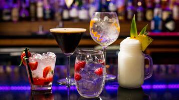 Um bar com diversas bebidas, incluindo um martini, um cocktail com gelo e fruta, e um jarro com um enfeite de abacaxi.