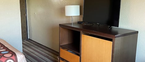 Quarto de hotel com uma cama, uma TV sobre um móvel de madeira e um tapete estampado.