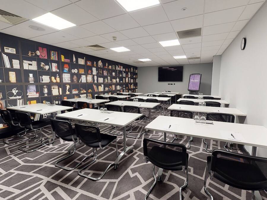 Uma sala de conferências com várias mesas e cadeiras, uma tela grande e uma parede decorada com diversos objetos.