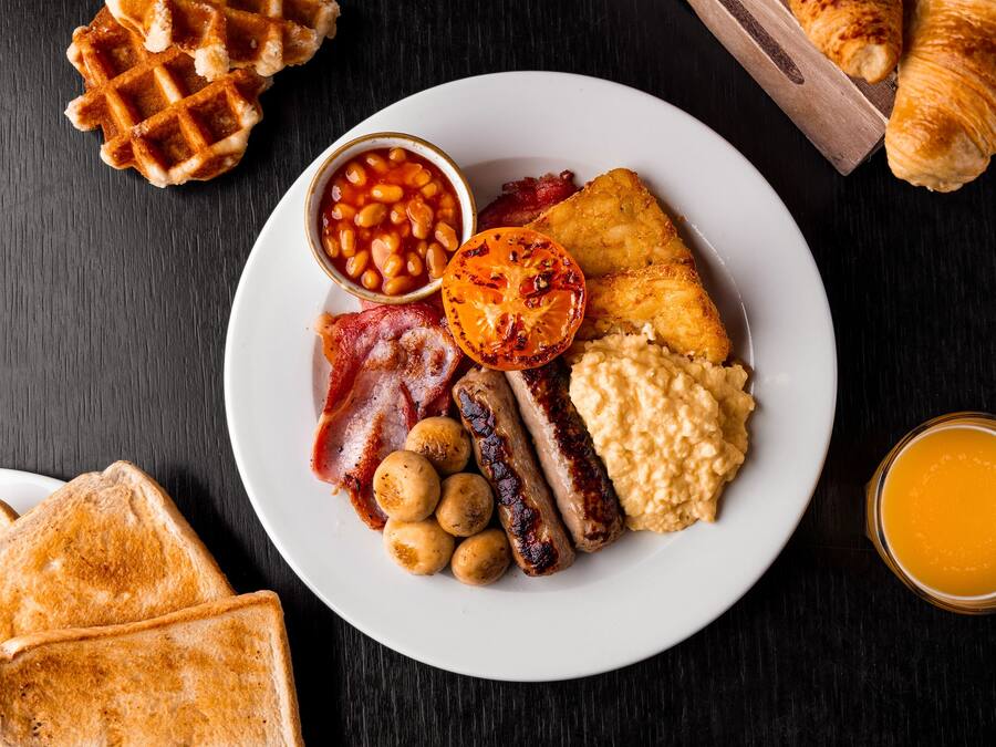 Prato de comida de café da manhã com torradas, linguiças, ovos, feijão e tomate grelhado.
