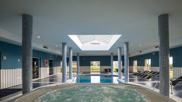Uma piscina interior com claraboia, colunas azulejadas e espreguiçadeiras.