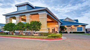 Um hotel com design moderno, com entrada coberta, área de estar externa e paisagismo bem cuidado.