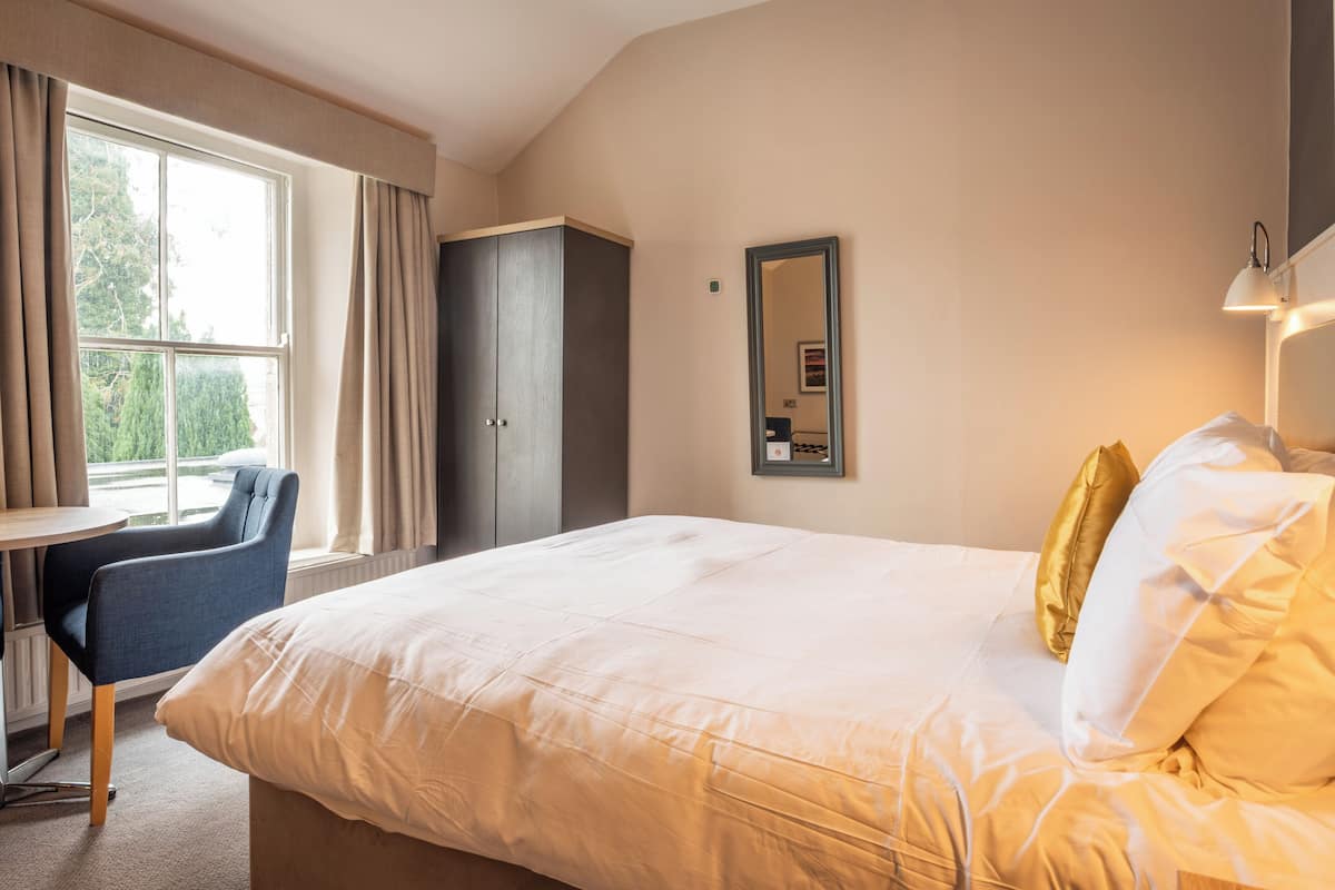 Quarto de hotel com cama, escrivaninha, cadeira, armário e espelho.