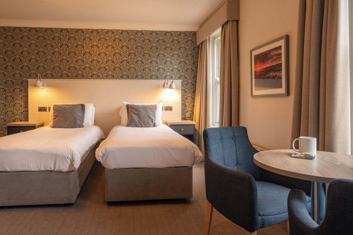 Quarto de hotel com duas camas, uma mesa pequena e uma cadeira.