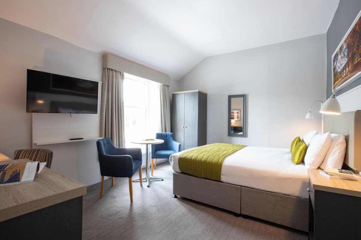 Quarto de hotel moderno com cama, escrivaninha, cadeira, televisão e guarda-roupa.
