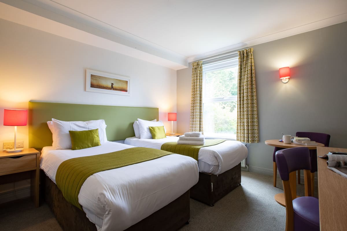 Quarto de hotel com duas camas, uma escrivaninha e uma cadeira.