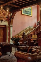 Um hall imponente com escada de madeira, assentos de couro, um lustre e um quadro na parede.