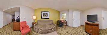 Quarto de hotel com escrivaninha, cadeira, televisão e sofá.