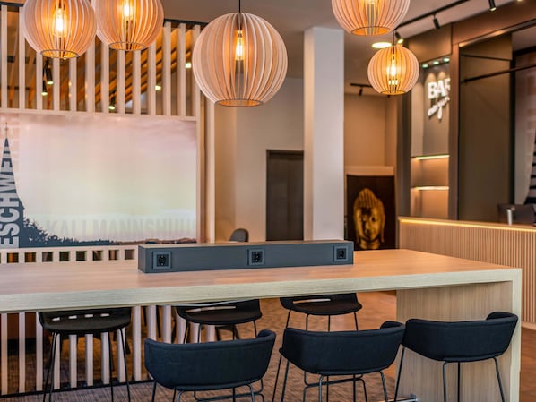Uma sala de conferência moderna com uma mesa comprida, quatro cadeiras pretas e três luminárias pendentes.