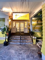 Entrada de um hotel com uma escadaria de pedra, uma placa com a inscrição 'Peninsula Bed & Cocktails' e uma palmeira ao fundo.